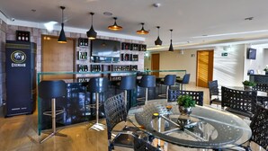 Uma área de bar moderna com mesa de vidro, banquetas e uma variedade de garrafas nas prateleiras.