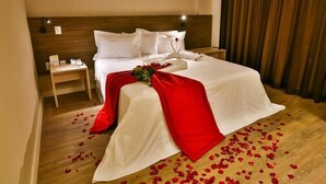 Quarto de hotel com cama bem arrumada, mesa de cabeceira com abajur e uma janela grande com cortinas.