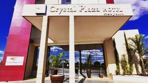 Exterior do Crystal Plaza Hotel com design arquitetônico moderno, destacando uma entrada imponente e plantas em vasos.