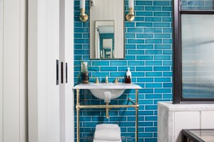 Casa de banho com lavatório branco, azulejos azuis, espelho e janela.