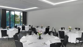 Uma sala de conferências com mesas redondas, cadeiras pretas e toalhas de mesa brancas.