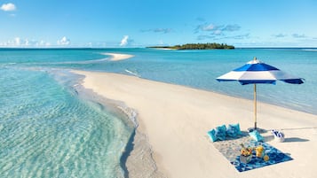 Uma praia com águas turquesa cristalinas, areal arenoso e um guarda-sol azul e branco.