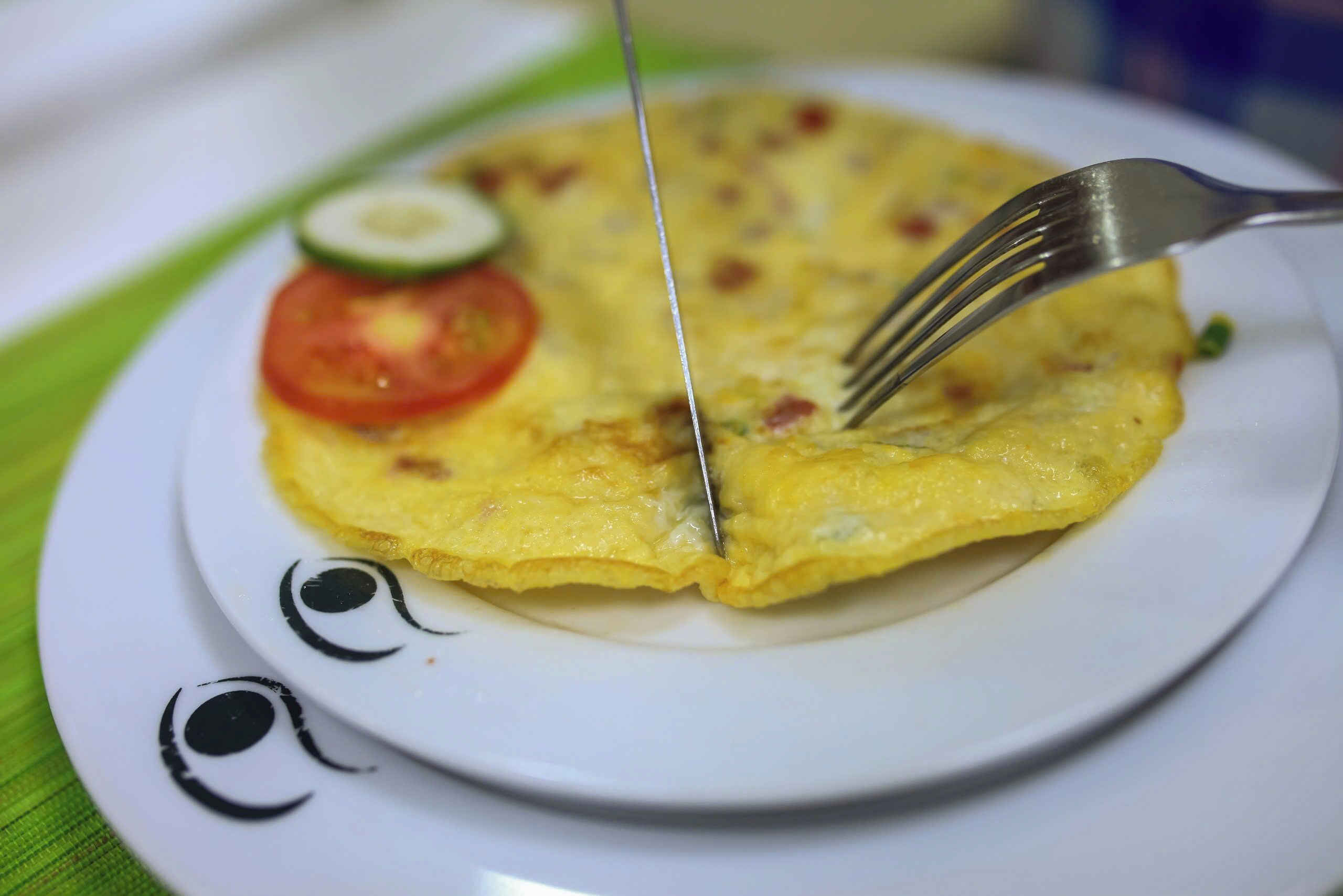 Um prato com omelete, uma fatia de tomate e pepino.
