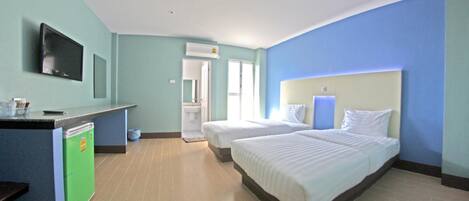 Quarto de hotel com duas camas, uma escrivaninha e televisão, e um banheiro visível por uma porta aberta.