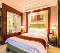 Quarto de hotel com uma cama grande, um espelho, duas fotos emolduradas na parede e uma mesa de cabeceira com uma luminária.