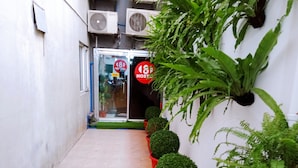 Um corredor estreito com entrada de albergue, plantas em vasos e unidades de ar condicionado na parede.