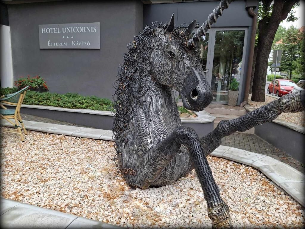 Escultura de metal de um cavalo em frente a um edifício com a placa 'HOTEL UNICORNIS'.