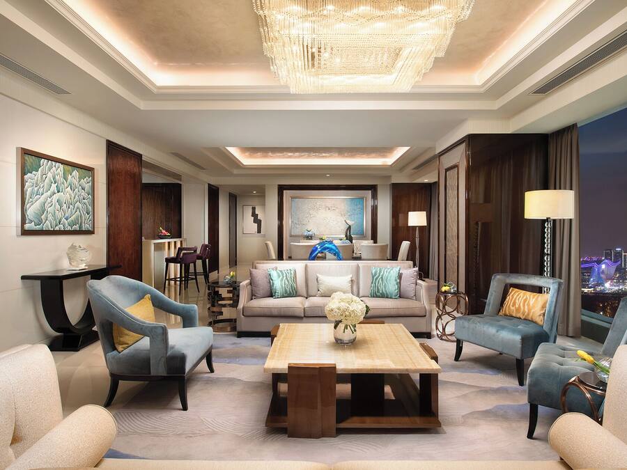 Uma sala de estar ampla com um candelabro, um conjunto de sofás e vista para a cidade à noite.