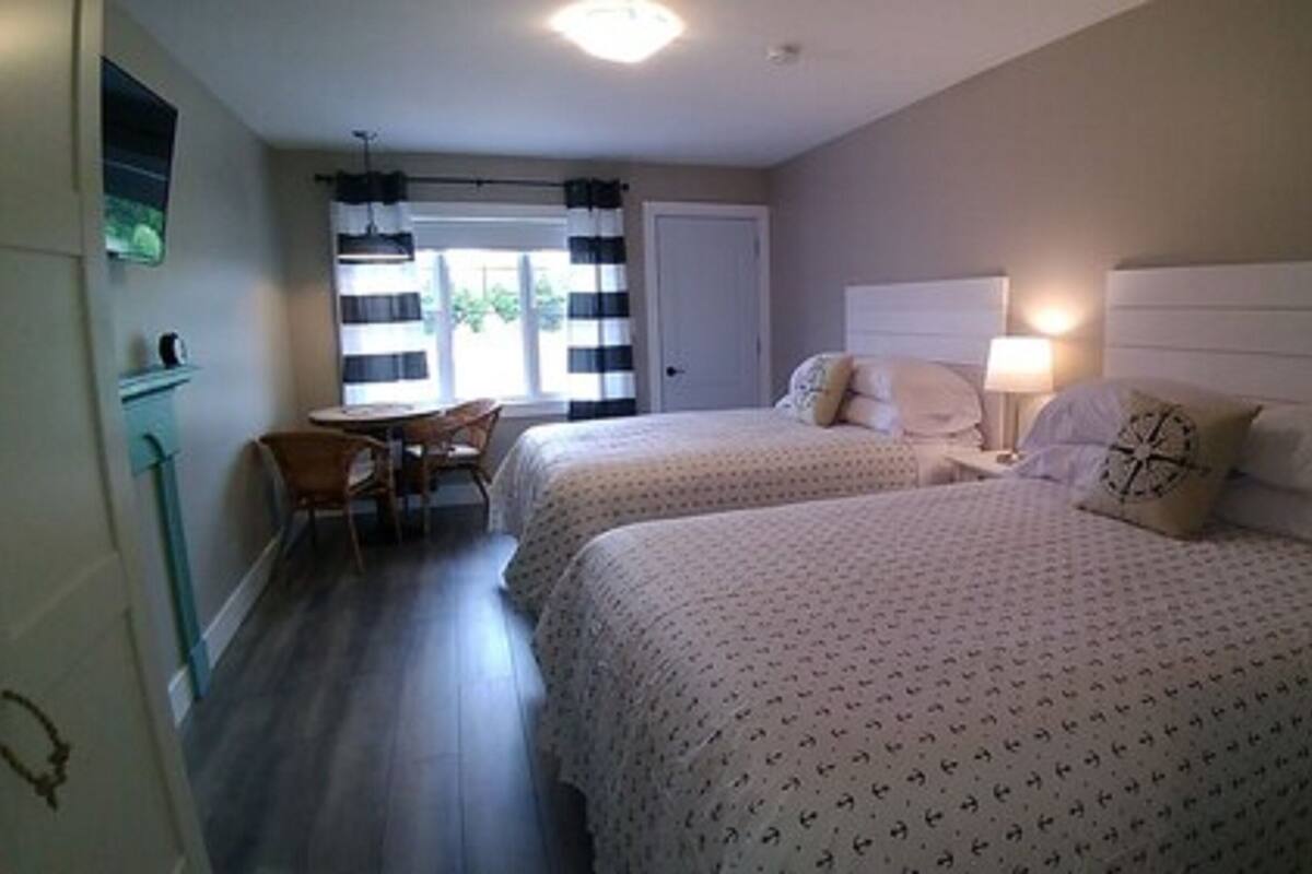 Quarto de hotel com duas camas, uma mesinha, cadeiras e uma janela com cortinas.