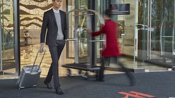 Um homem de terno, com mala, entra em um hotel com entrada de vidro e placa indicando Marriott Hangzhou Qianjiang.