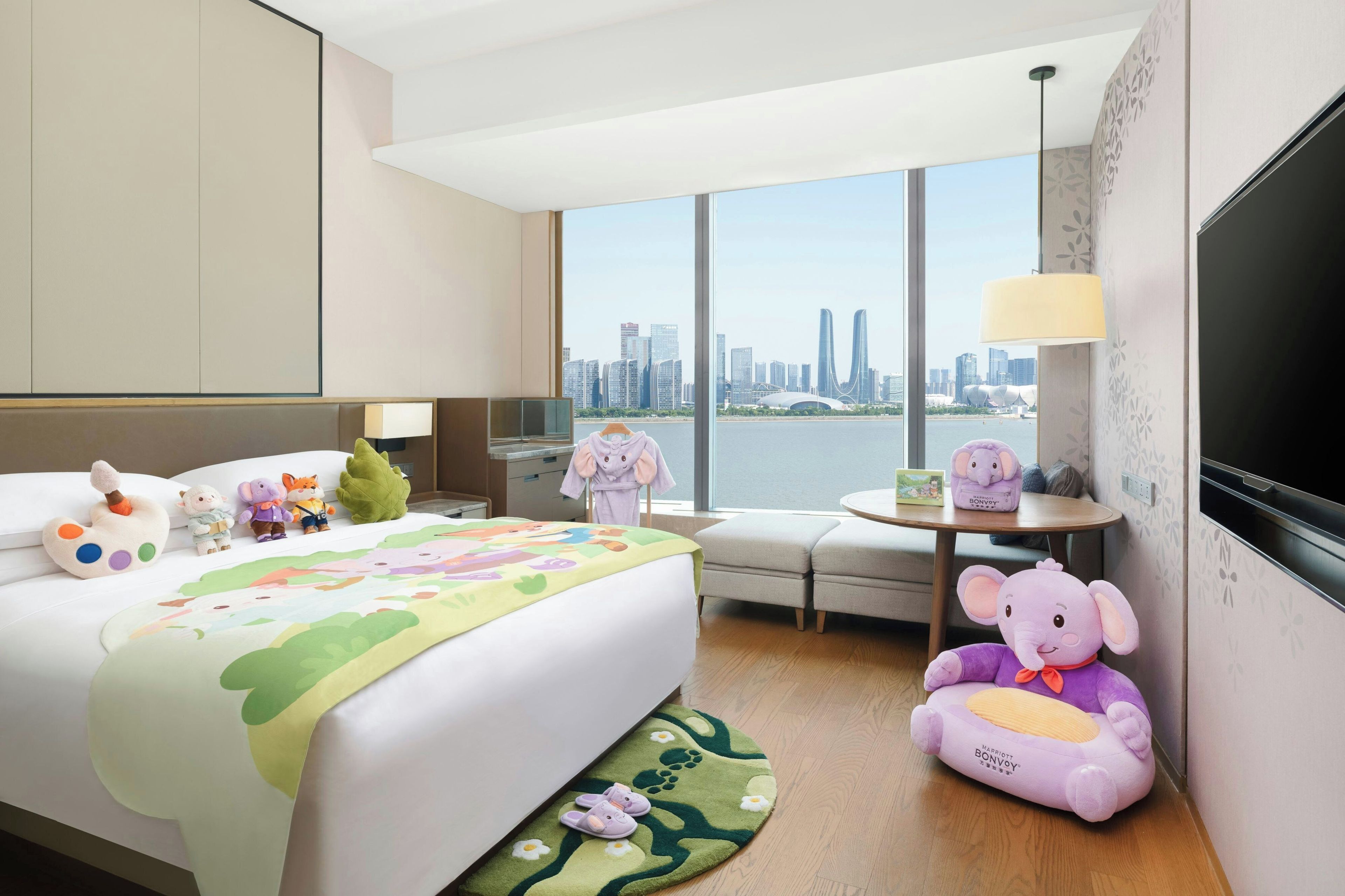 Quarto de hotel com cama grande, vista para o horizonte urbano, TV de tela plana e pequena mesa com abajur.