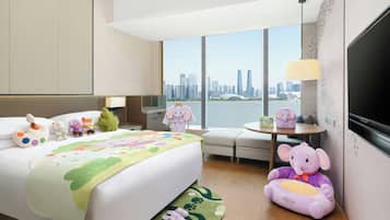 Quarto de hotel com cama grande, vista para o horizonte urbano, TV de tela plana e pequena mesa com abajur.