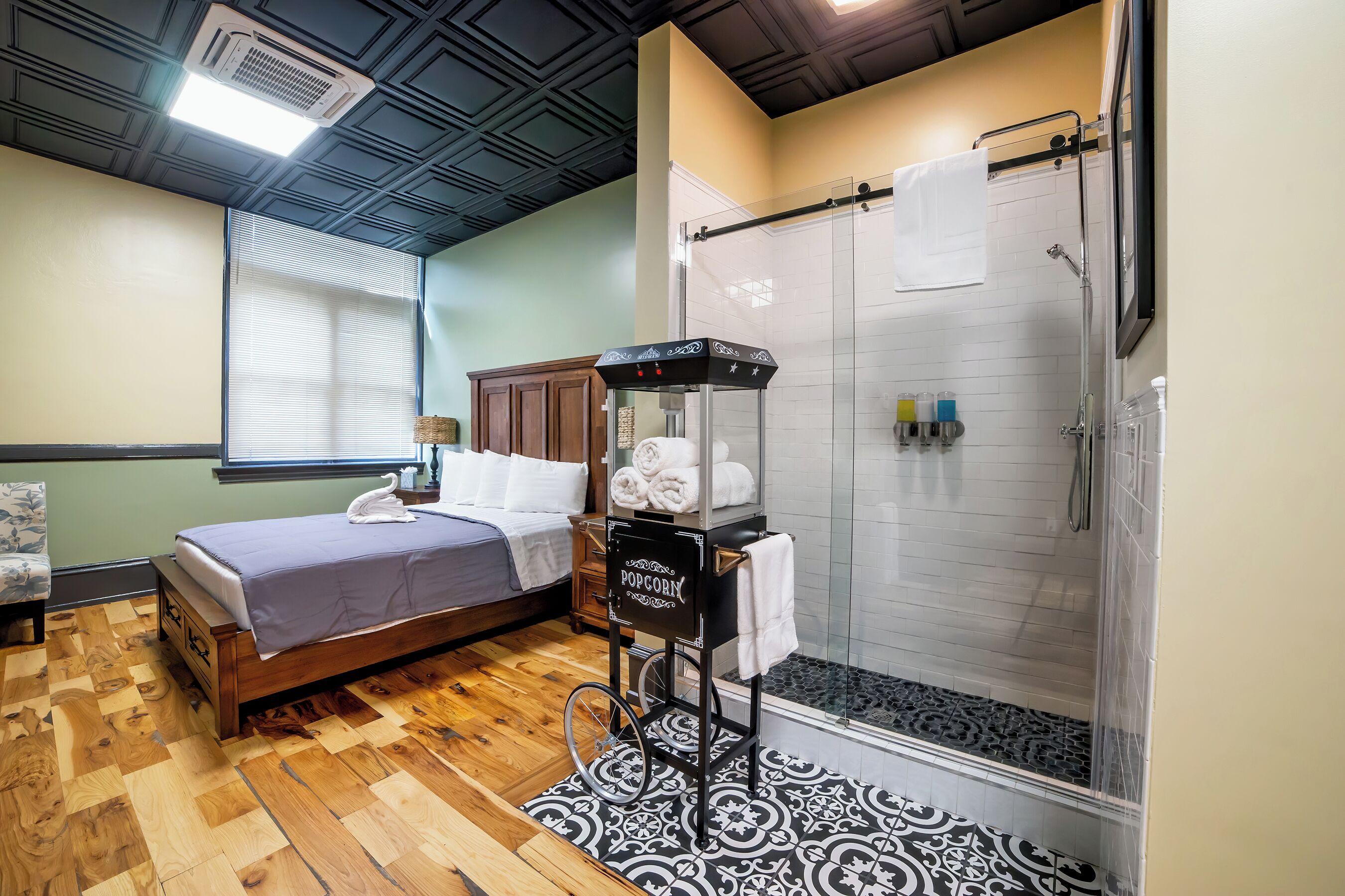 Quarto de hotel com cama, chuveiro e um carrinho de pipoca.