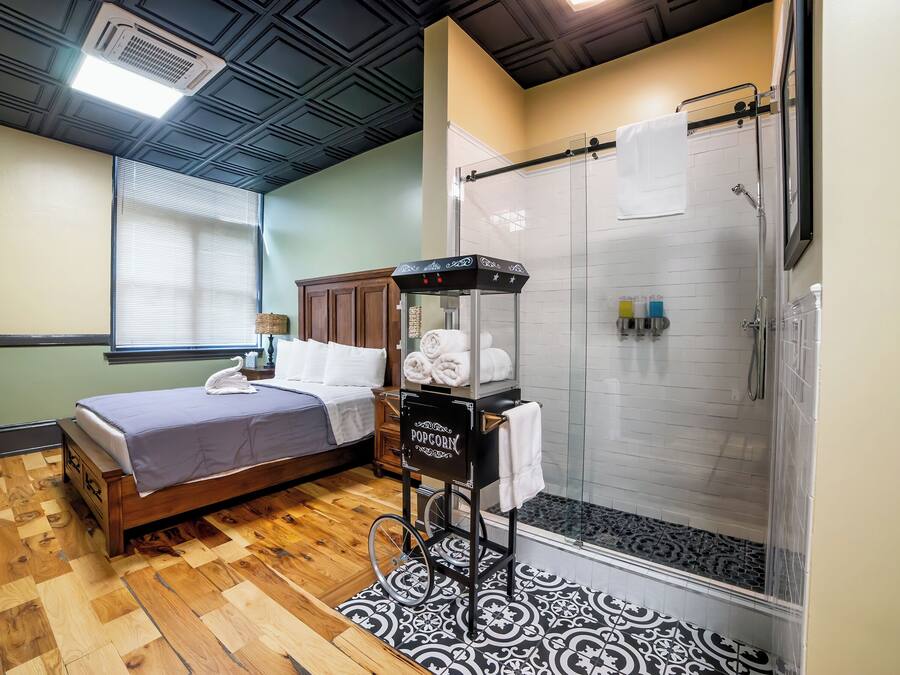 Quarto de hotel com cama, chuveiro e um carrinho de pipoca.