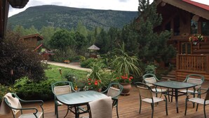 Um deck de madeira com área de estar ao ar livre, rodeado por vegetação exuberante e vista para uma montanha arborizada.