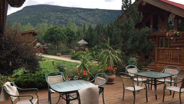 Um deck de madeira com área de estar ao ar livre, rodeado por vegetação exuberante e vista para uma montanha arborizada.