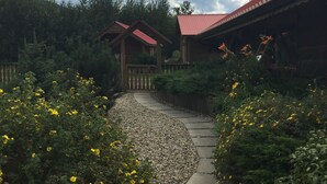 Um caminho leva a cabanas de madeira com telhados vermelhos, cercadas por vegetação e flores amarelas.