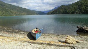 Um lago calmo com um pequeno barco na margem, cercado por montanhas arborizadas.