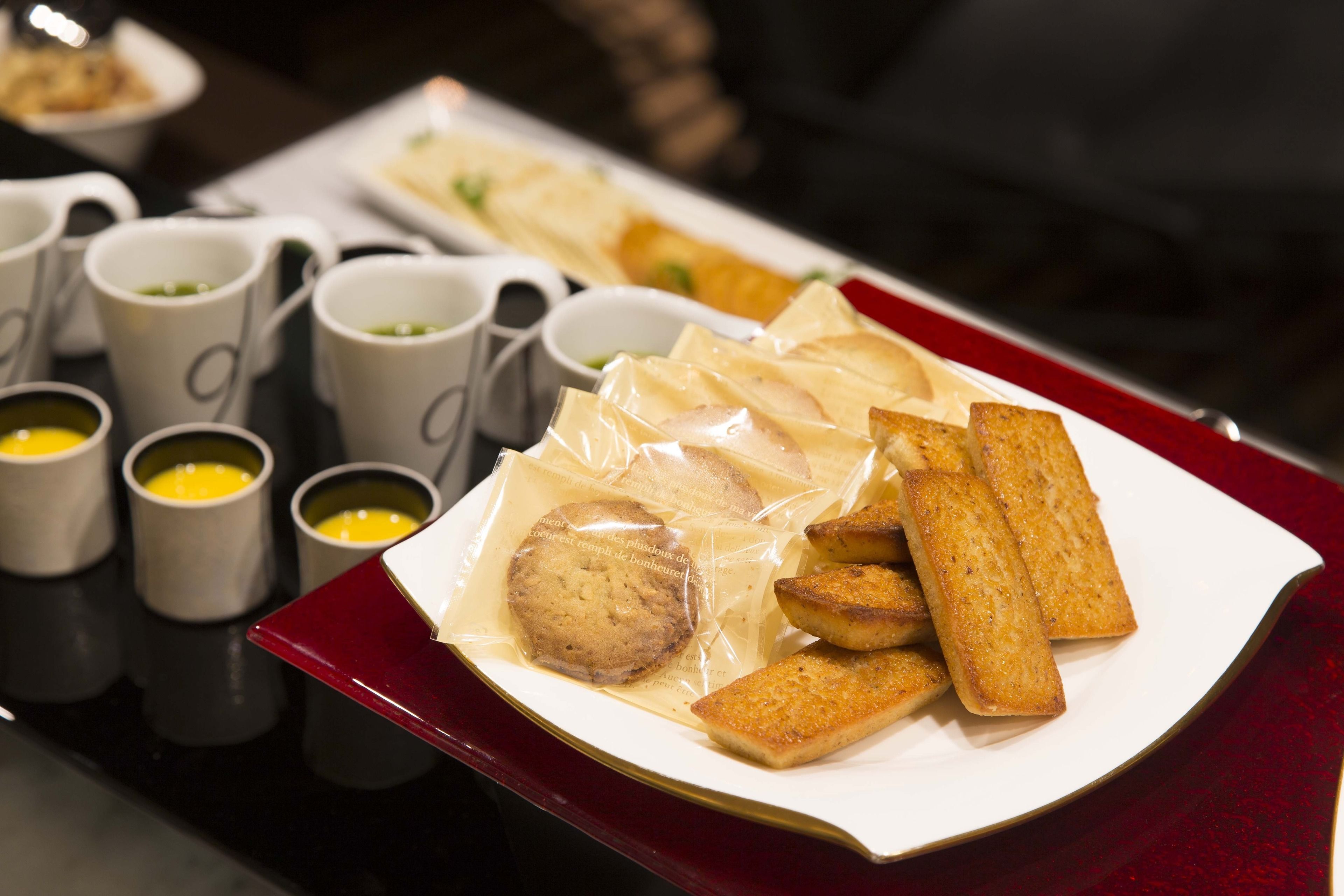 Uma bandeja com diversos alimentos, incluindo pão e biscoitos, acompanhada de pequenos copos com molhos.