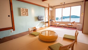 Um quarto tradicional japonês com piso de tatame, uma mesa baixa com almofadas, uma cadeira de vime trançado e uma grande janela com vista para o mar.