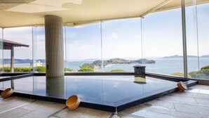 Piscina interior moderna com cobertura de vidro, grandes janelas e vista para a paisagem costeira.