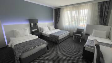Quarto de hotel com duas camas, uma escrivaninha, uma cadeira e uma janela grande com cortinas.