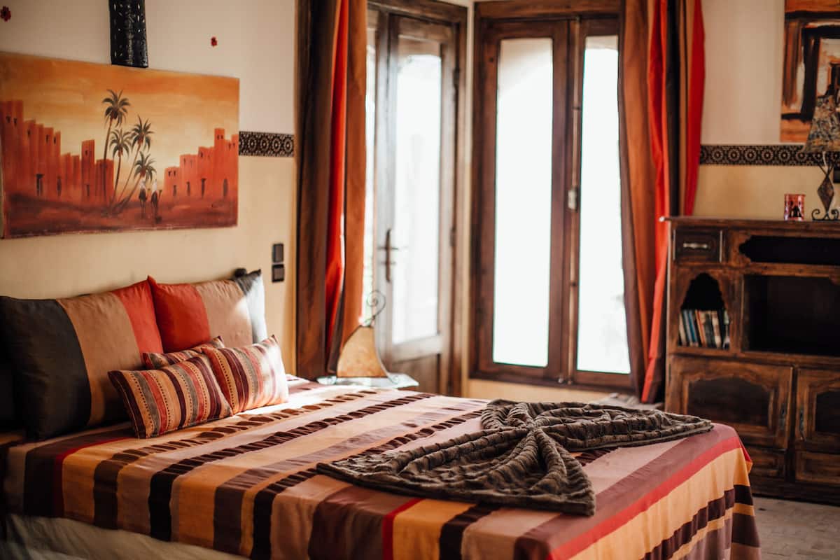 Quarto com cama, um quadro, um armário de madeira e janela com cortinas.