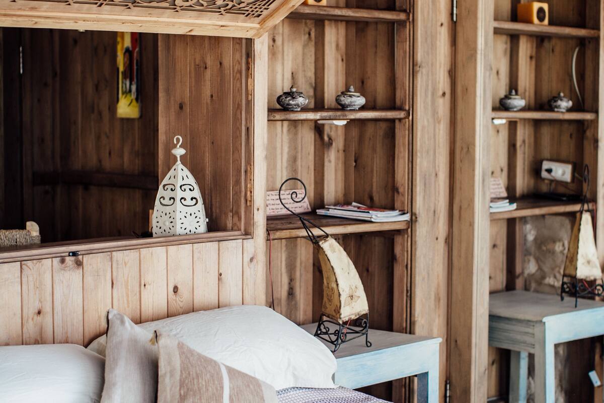 Um quarto de madeira com uma cama, estantes e um espelho.