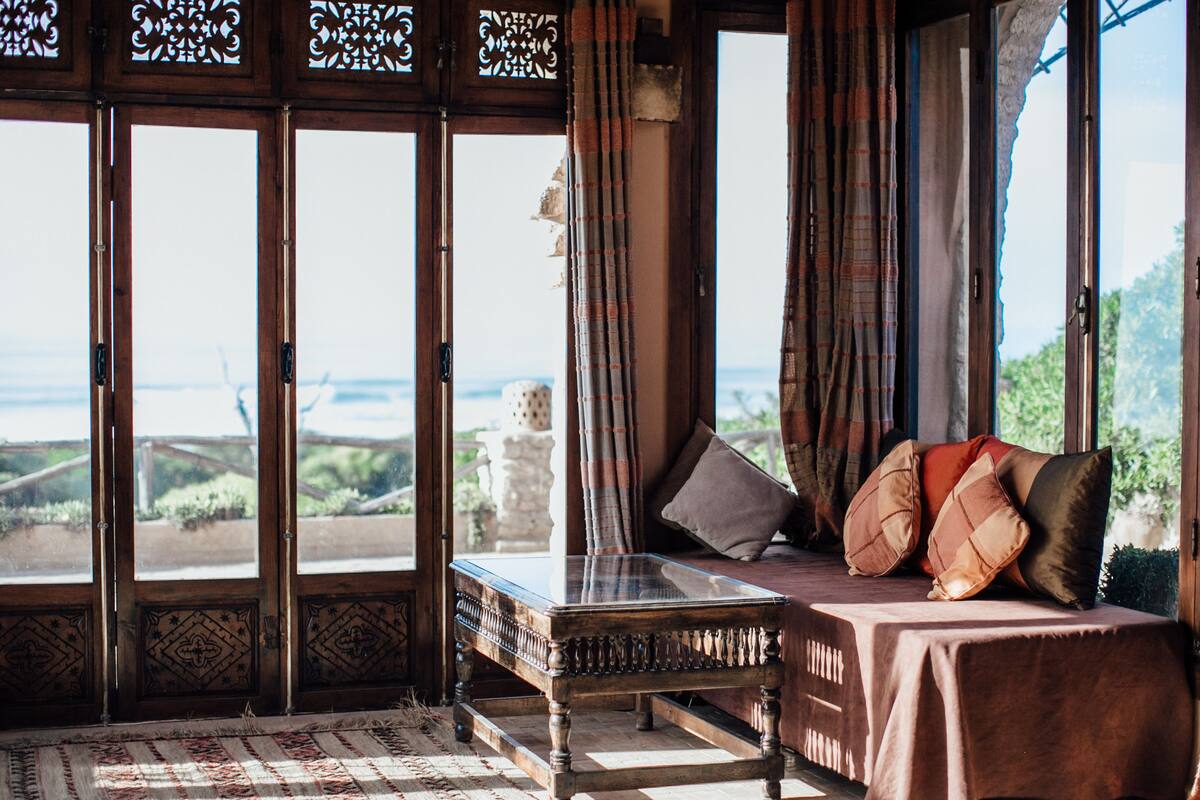 Quarto tradicional com uma cama, uma mesa de madeira e vista para o mar.