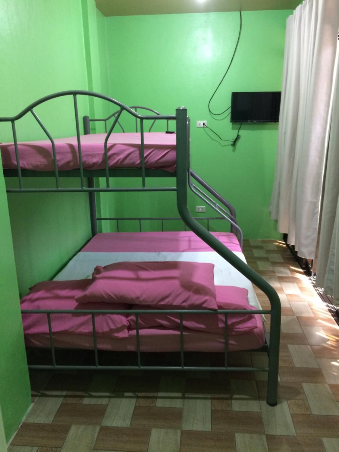 Uma cama beliche com roupa de cama rosa em um quarto com paredes verdes e chão de azulejos.