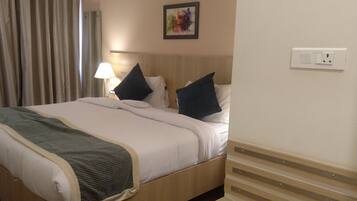 Quarto de hotel com uma cama, uma luminária, um quadro na parede e uma tomada.