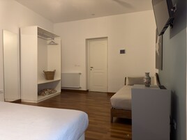 Quarto com cama, guarda-roupa, radiador, porta e uma pequena mesa com um vaso.