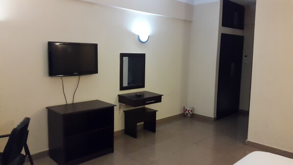 Quarto de hotel com televisão de tela plana, uma pequena escrivaninha com espelho, uma cadeira e uma cama.