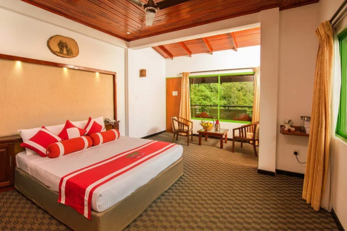 Quarto de hotel com cama, teto de madeira, janela com vista para o verde e uma pequena mesa com cadeiras.
