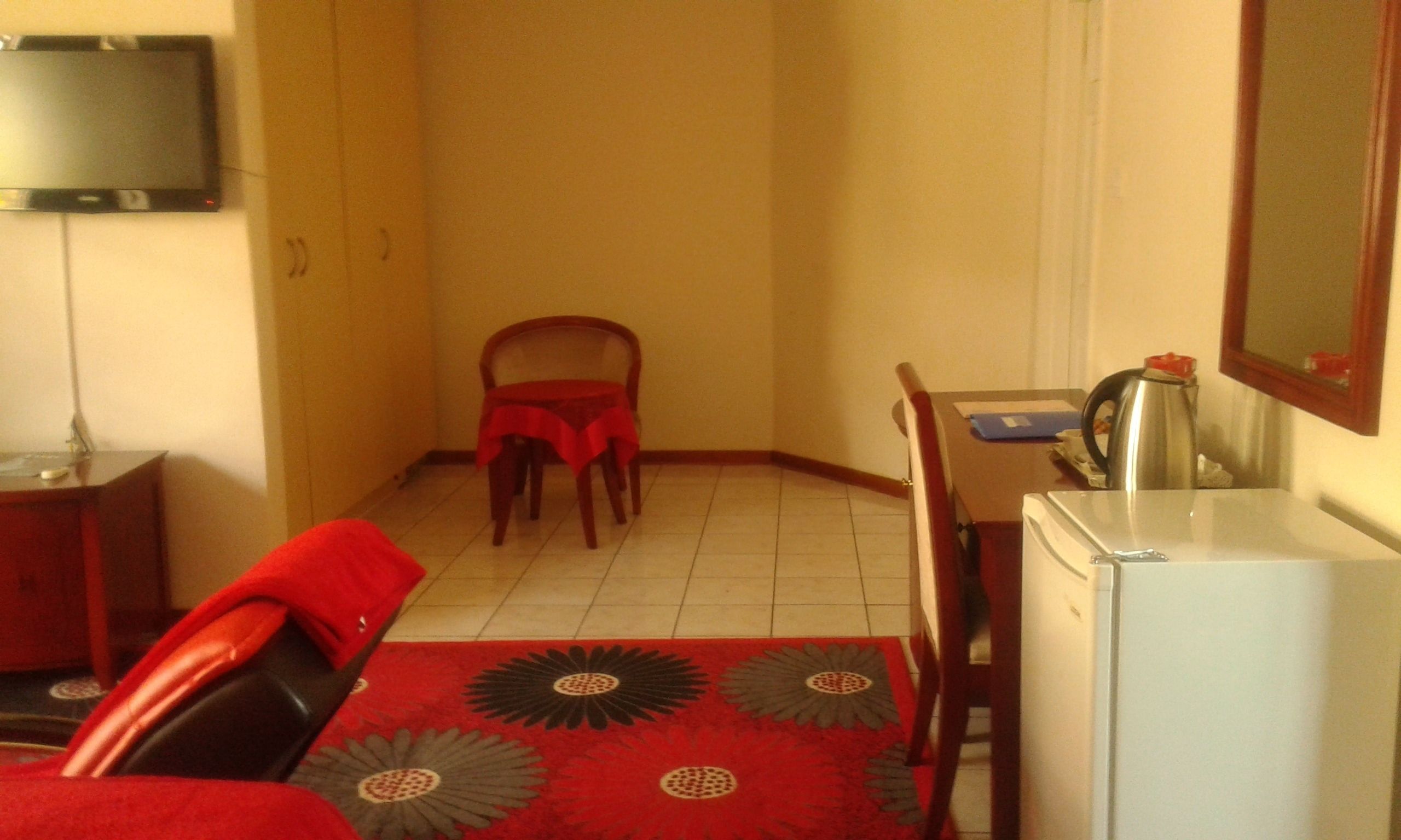 Quarto de hotel compacto com um pequeno espaço de refeições, televisão na parede e um frigorífico.
