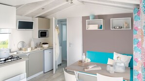Cozinha moderna com micro-ondas, fogão e pia. Há uma área de refeições com mesa, cadeiras e um sofá azul. Prateleiras com objetos decorativos na parede.