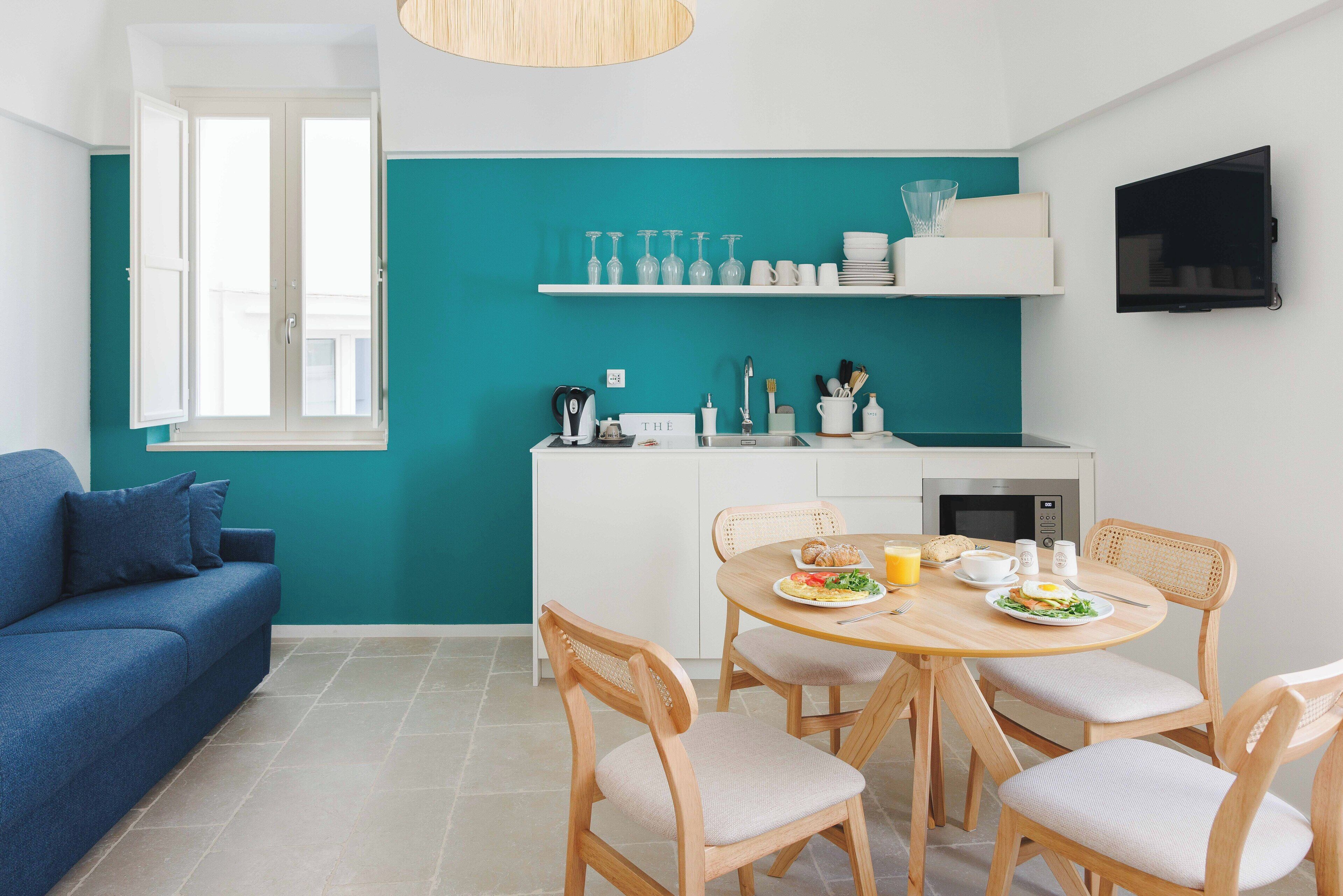 Cozinha moderna com paredes verde-água, armários brancos e uma área de jantar com cadeiras e mesa de madeira.
