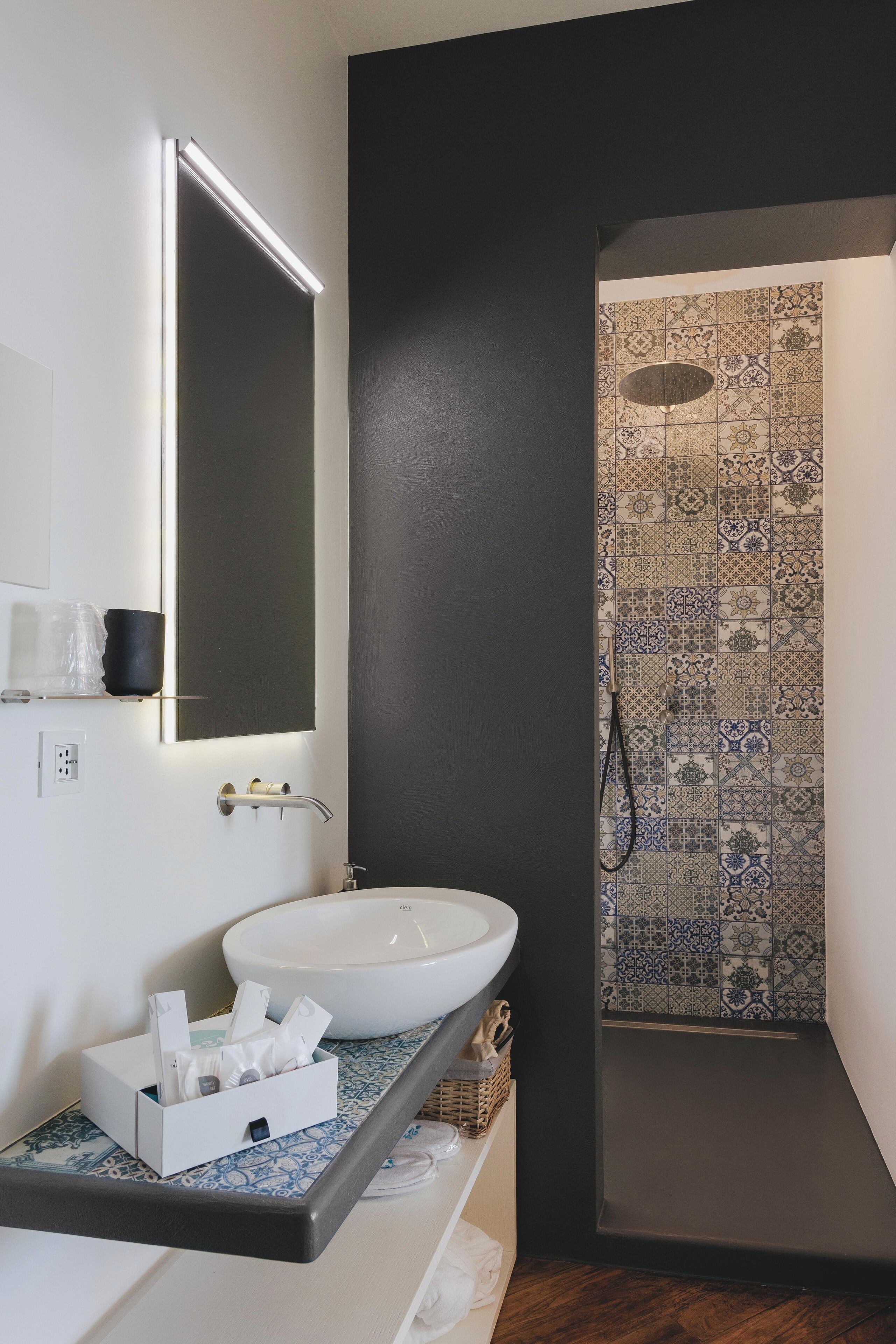 Um banheiro moderno com pia branca, espelho e chuveiro com azulejos estampados.