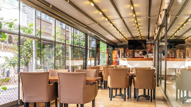 Um café moderno com grandes janelas, plantas dentro e piso revestido de azulejos.
