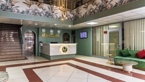 Um hall de hotel com balcão de recepção, escada, sofá verde e televisão.