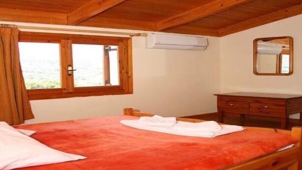 Quarto com cama de madeira, cômoda de madeira, espelho e ar condicionado.