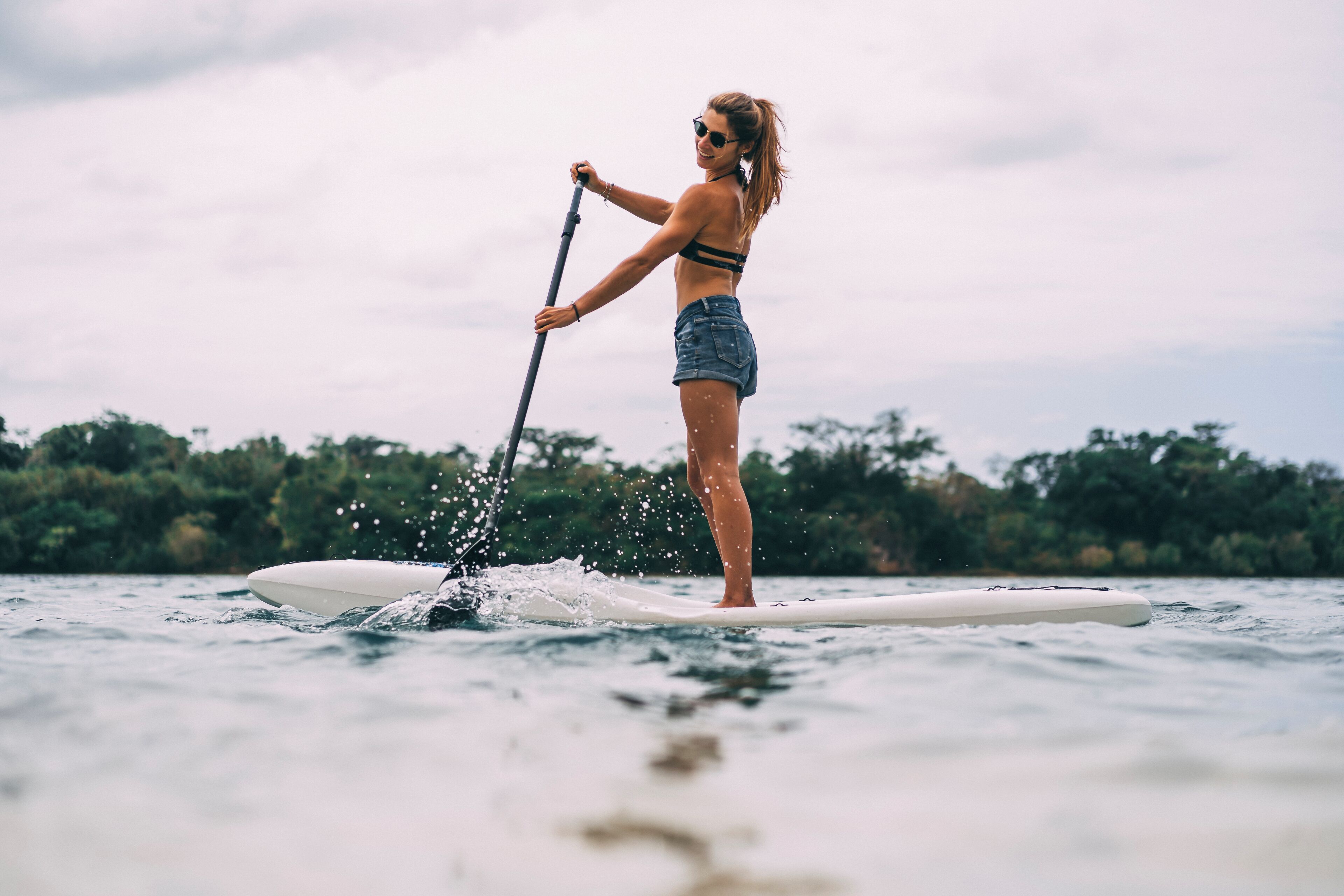 Uma pessoa praticando paddleboard em águas calmas, com árvores ao fundo.