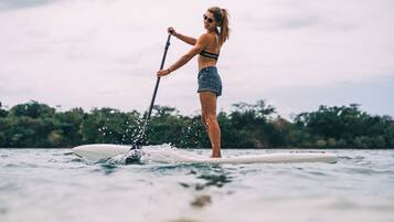 Uma pessoa praticando paddleboard em águas calmas, com árvores ao fundo.