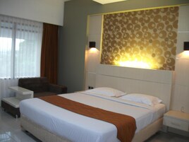 Quarto de hotel com uma cama grande, uma mesinha de cabeceira, uma cadeira e parede estampada.