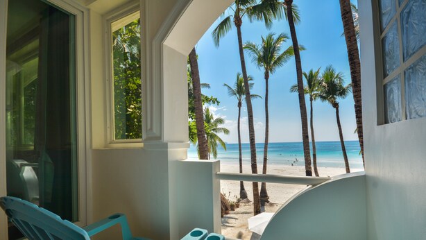 Quarto com vista para a praia, com janela, uma cadeira e uma mesinha.