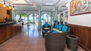 Um hall de entrada com balcão de recepção, móveis de vime, uma pintura grande e vista para o oceano.