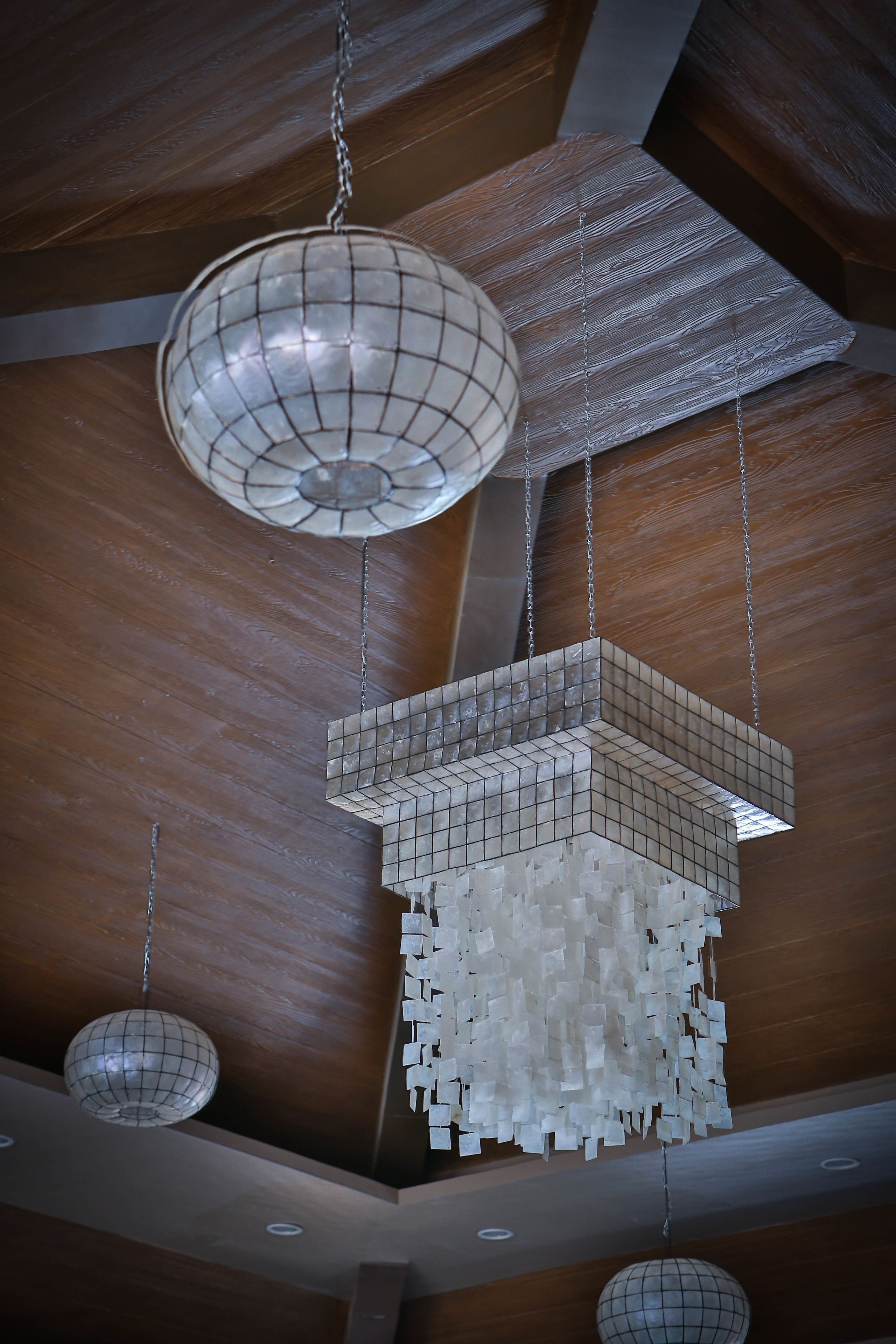 Teto com painéis de madeira, luminárias esféricas penduradas e luminária pendente geométrica.