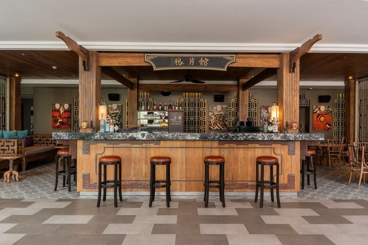 Uma área de bar com balcão de madeira, banquetas e um letreiro acima.