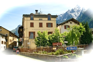 Hotel chamado "Albergo Piz Cam" com montanhas ao fundo.