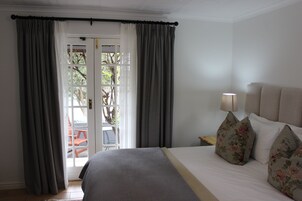 Um quarto com cama, cortinas, abajur e vista através de uma porta.